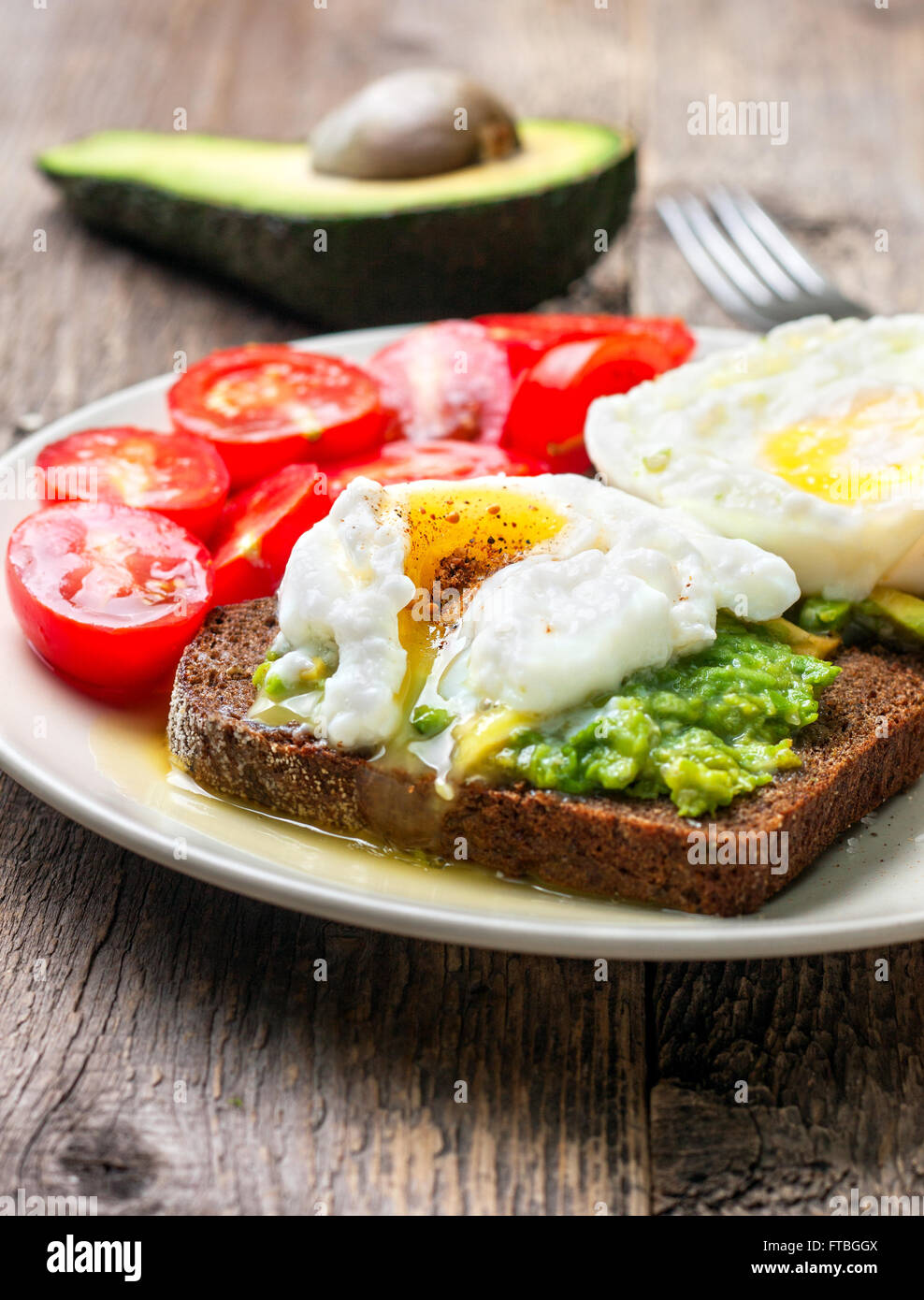 Open toast with avocado and egg, cherry tomatoes on a wooden background ...