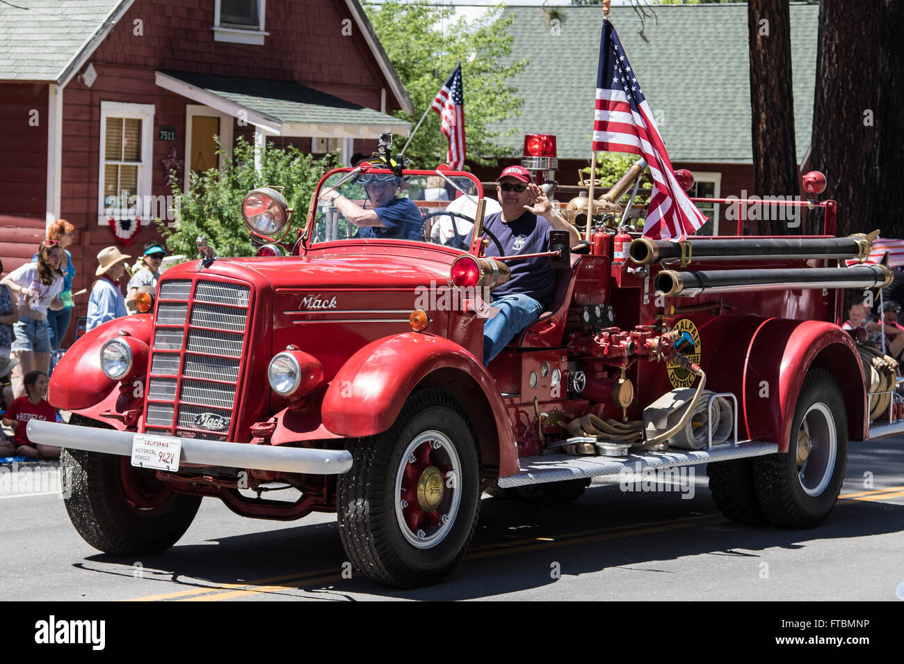Firemen aboard a vintage fire engine driving in a parade smile and wave ...