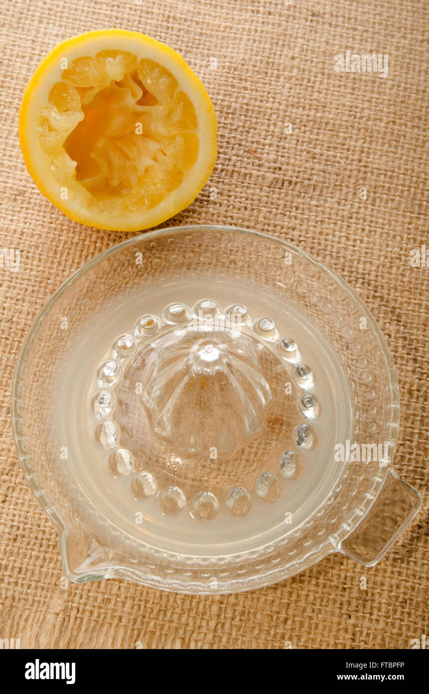 squeezed lemon, glass lemon squeezer and fresh lemon juice on jute ...