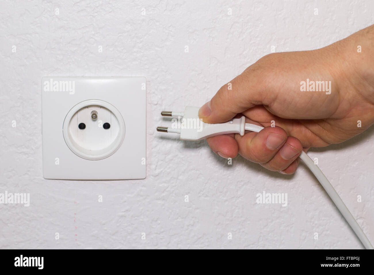 Hand plugs electrical cord in white wall socket Stock Photo - Alamy