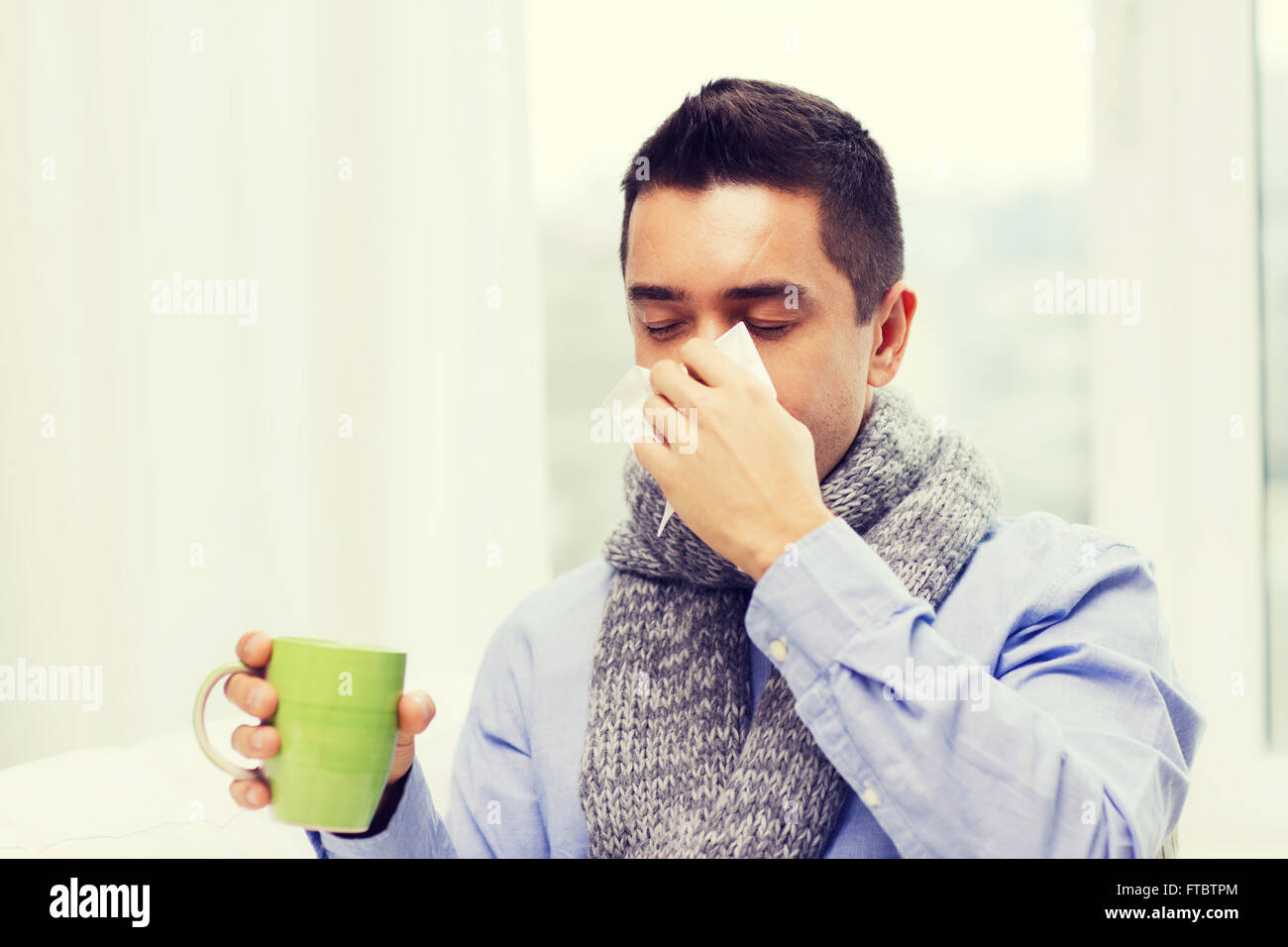 ill man with flu drinking tea and blowing nose Stock Photo - Alamy