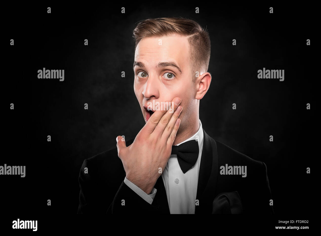Portrait of surprised man in suit with bow-tie over dark background ...
