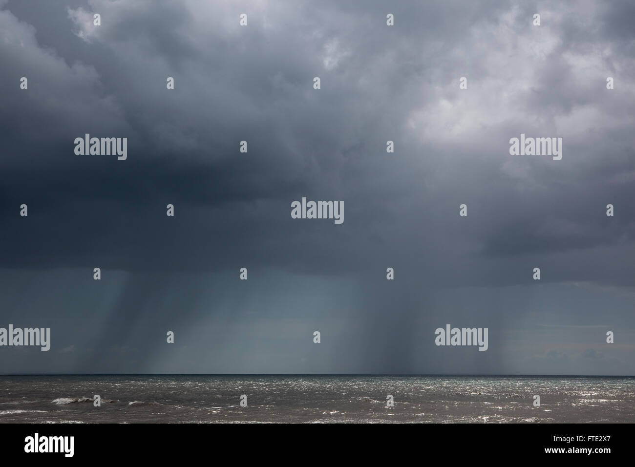 A heavy rain storm out at sea turns the sky deep dark grey as the rain ...