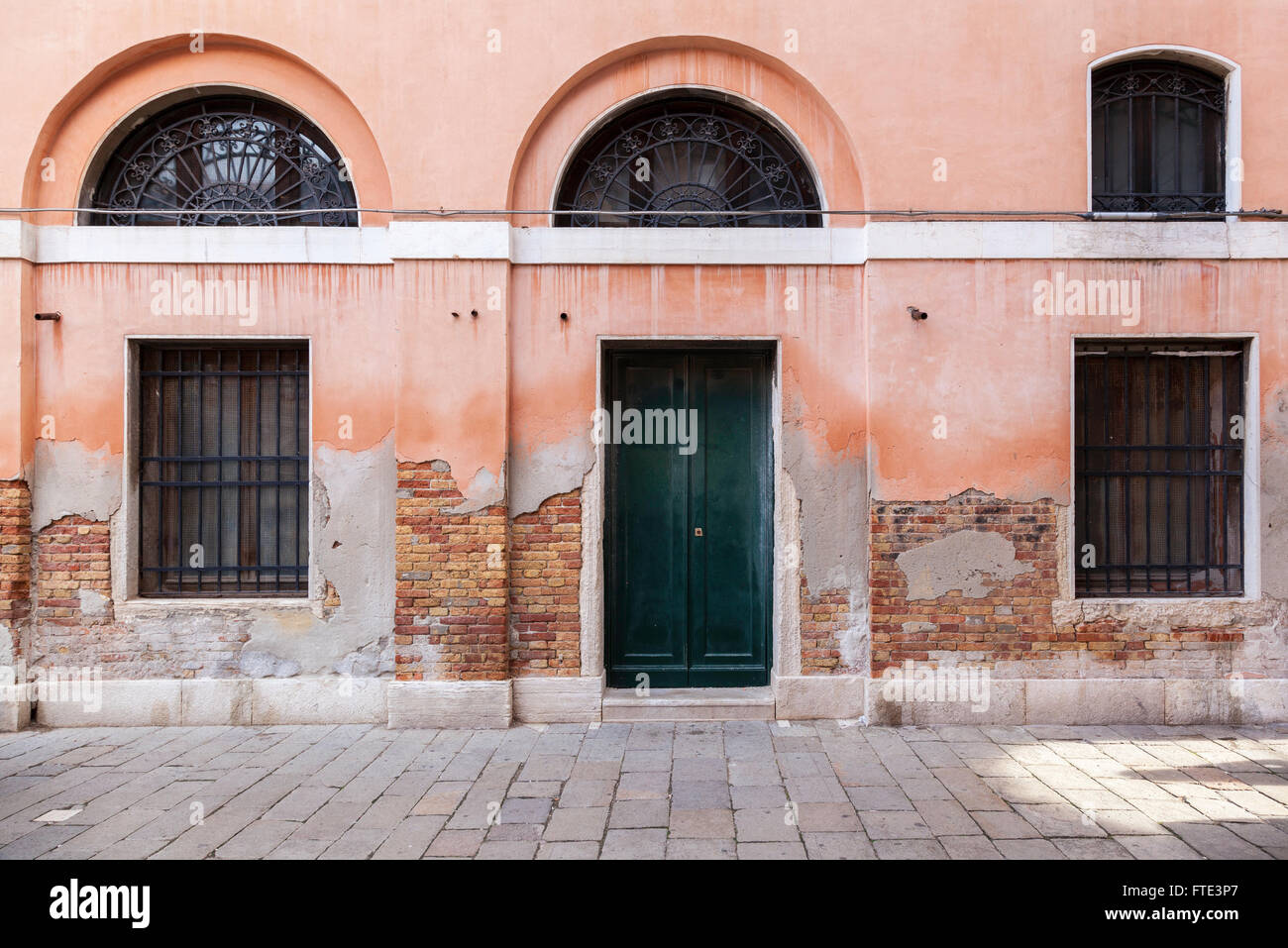 Frontage of a decaying building with arched windows, crumbling pink ...