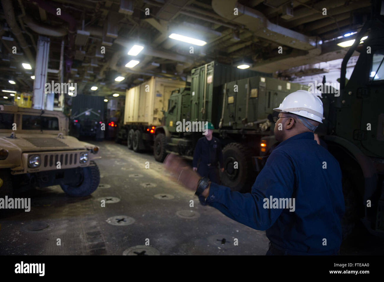 A sailor directs a Humvee in the well deck of the USS Bataan (LHD 5), a ...