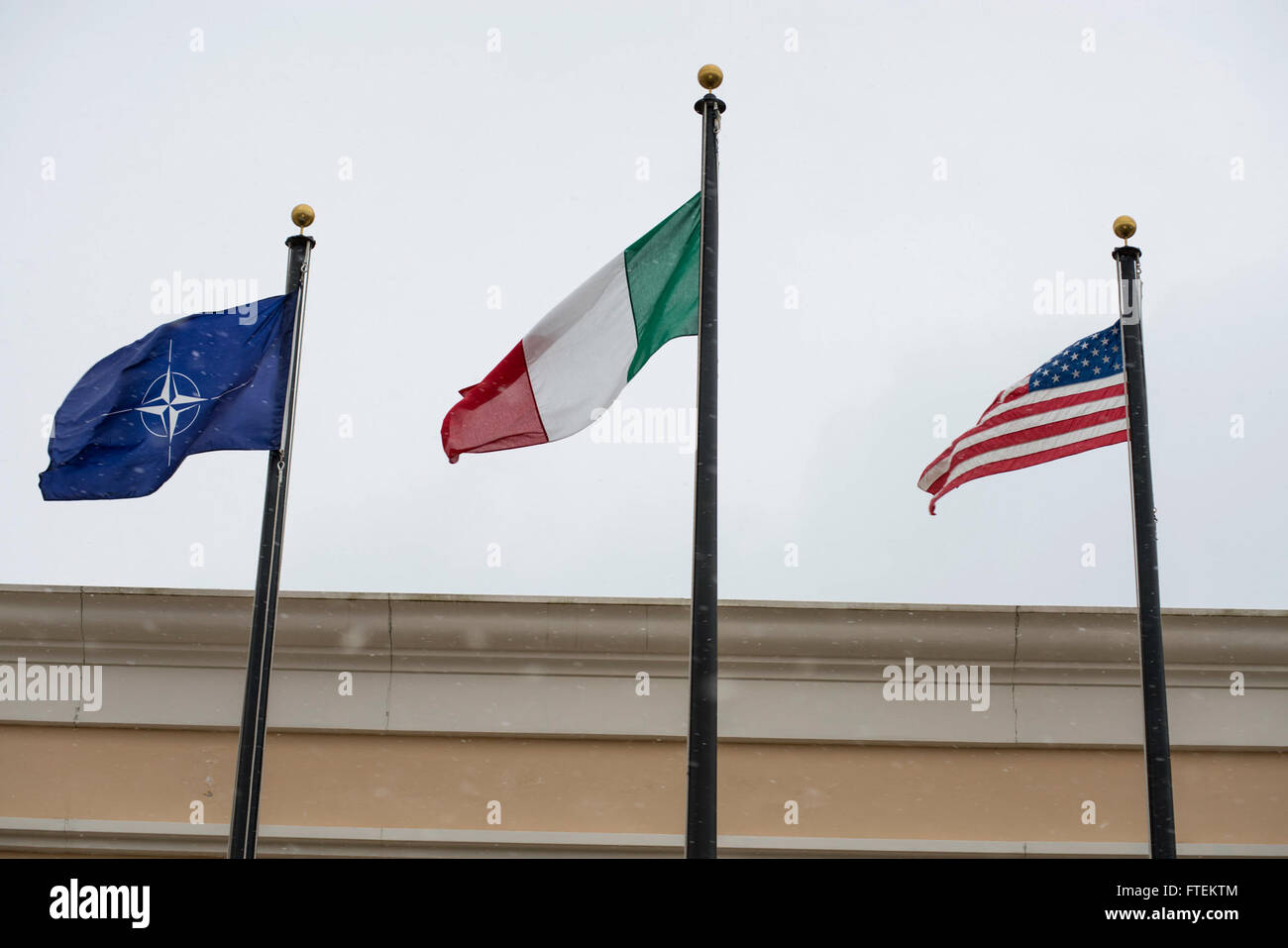 The NATO flag, Italian ensign, and U.S. ensign fly in the snow at Naval ...