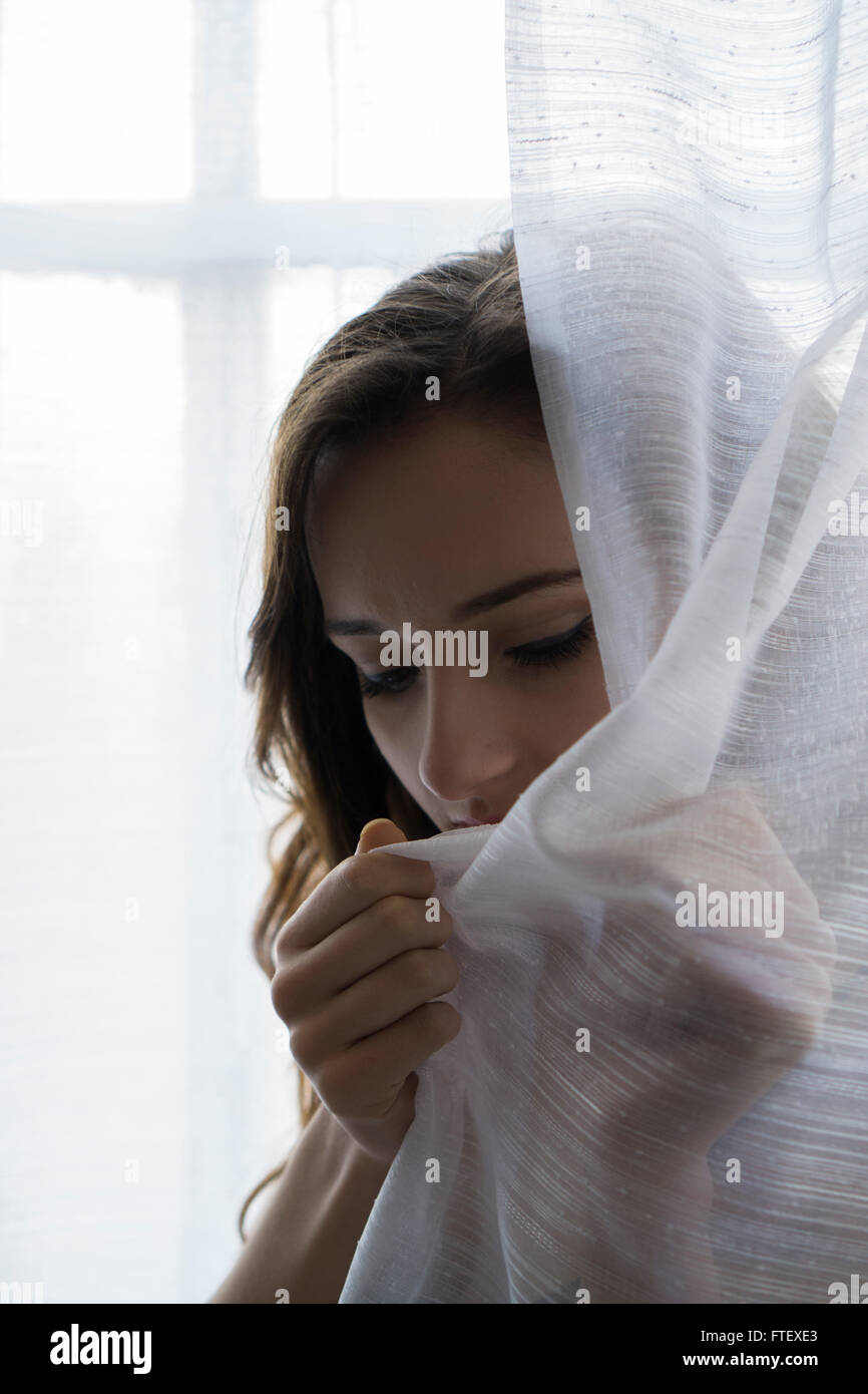 Serious young woman hiding behind the curtains by the window Stock ...