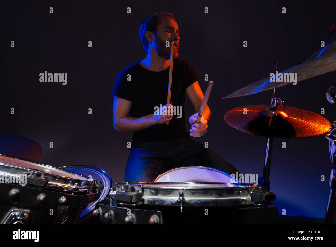 Handsome bearded man drummer sitting and plaing on drums over dark ...