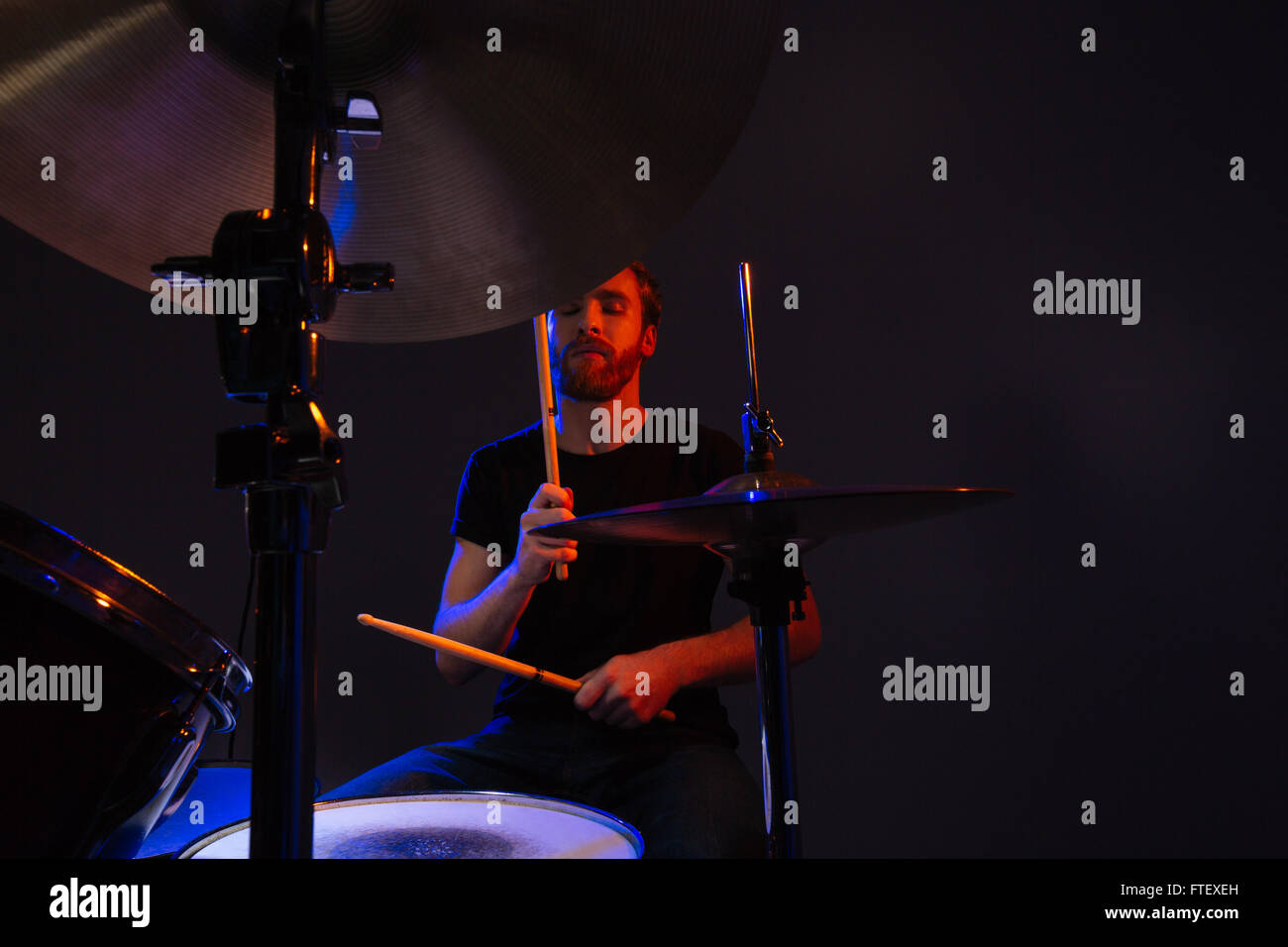 Attractive bearded man drummer with closed eyes enjoying playing drums ...