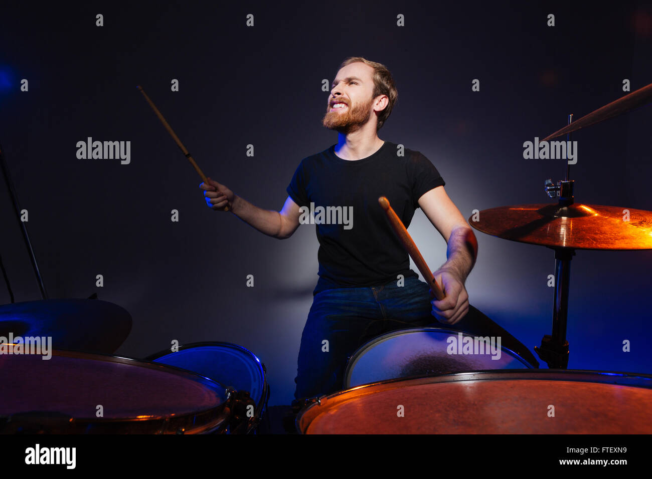 Brutal excited young man drummer with beard playing drums over dark ...