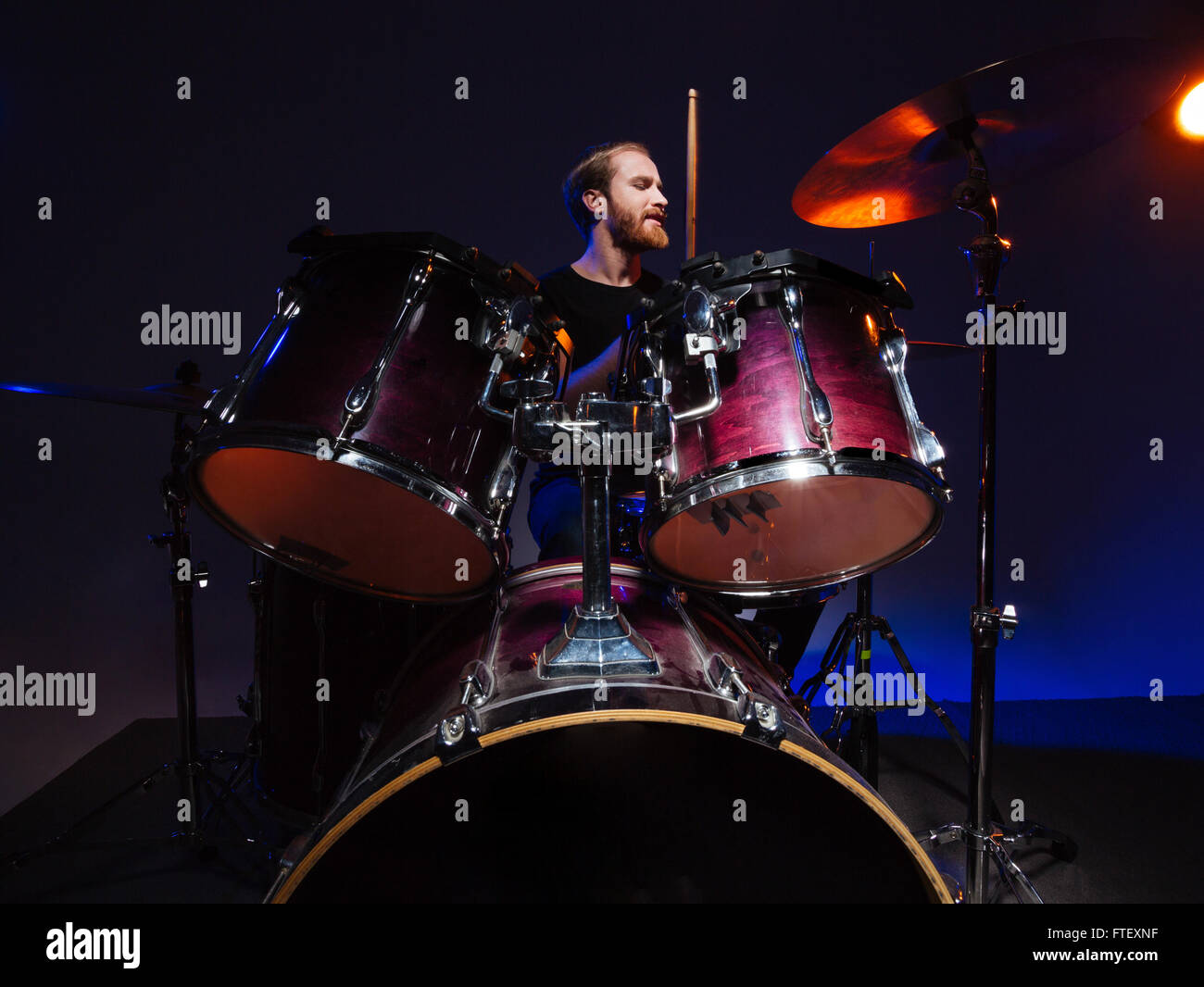 Attractive bearded man drummer sitting and playing on his kit over dark ...