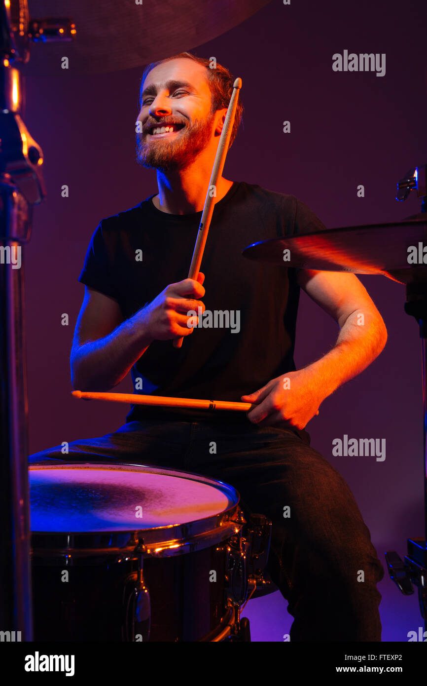 Happy cheerful bearded man drummer playing on his kit with sticks over ...