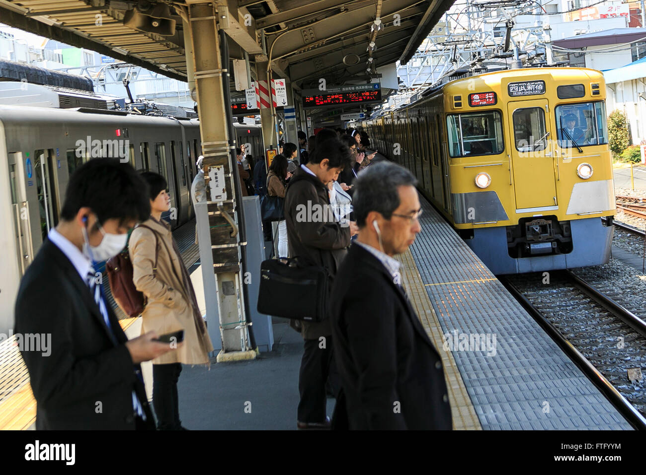 Passengers wait to aboard a yellow Seibu train at Kami-Shakujii station ...
