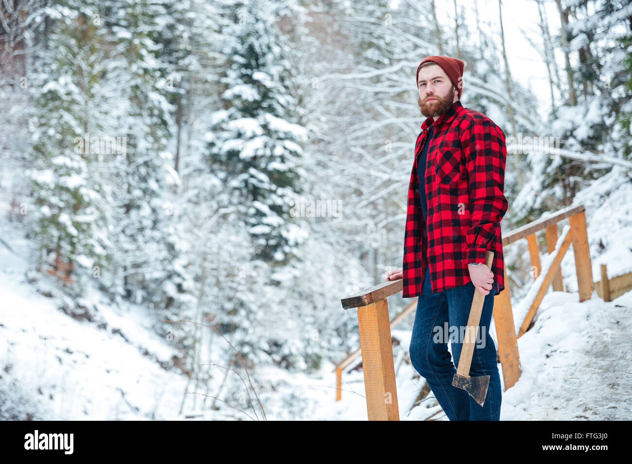 Handsome pensive young man with axe standing in mountain winter forest ...