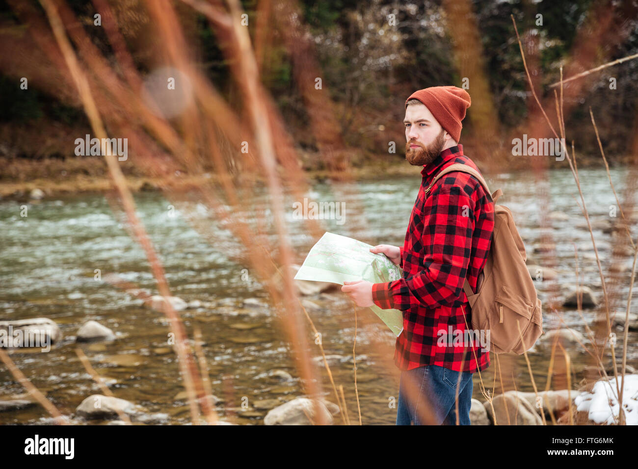 Male hiker holding map and looking away outdoors with river on ...