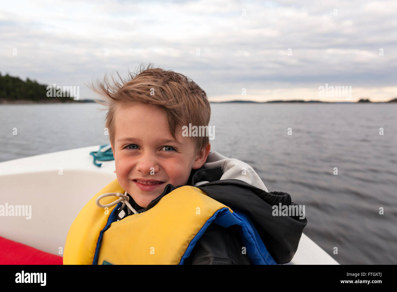 Young boy wearing a life vest at the front of a motor boat at sea ...