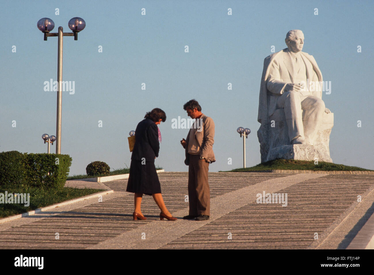A couple talking beside large statue of the dictator Enver Hoxha ...