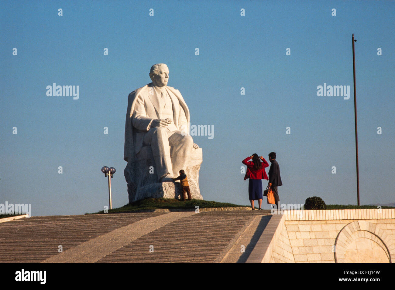 A couple talking beside large statue of the dictator Enver Hoxha ...