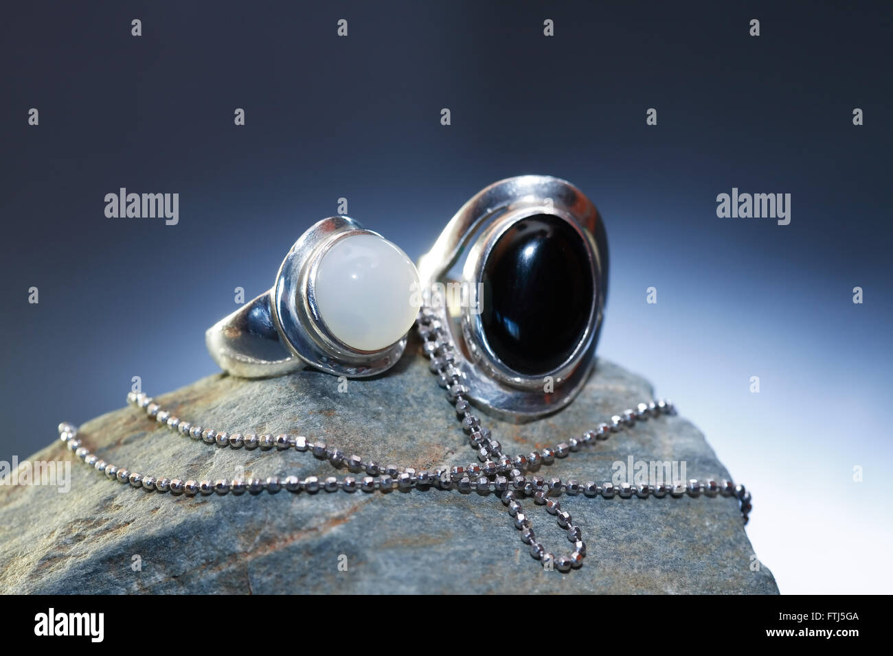Silver rings with gem near chain on gray stone against nice dark ...