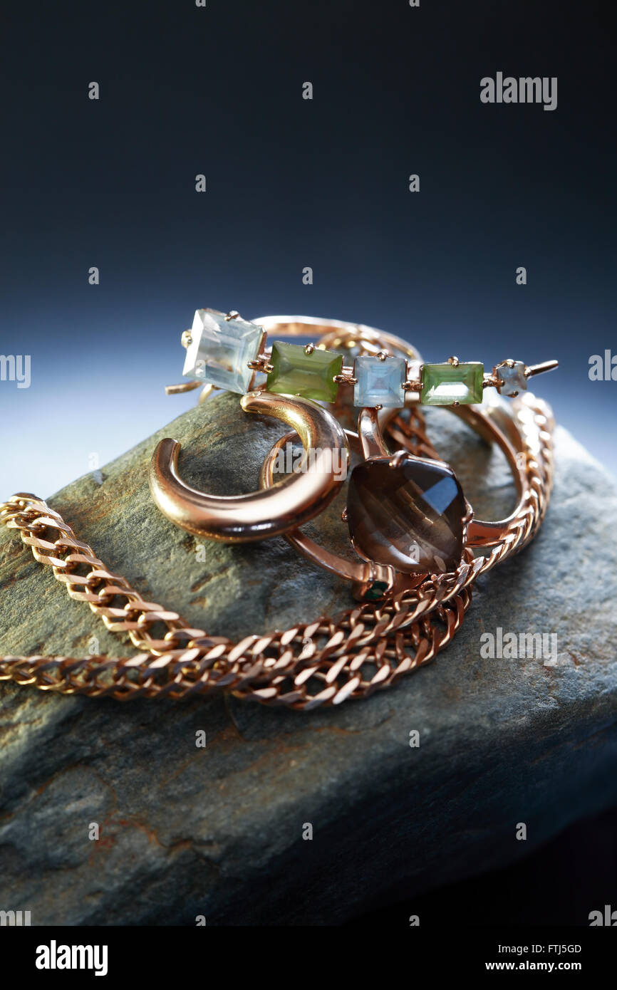 Set of various gold jewelry adornments on stone against dark background ...