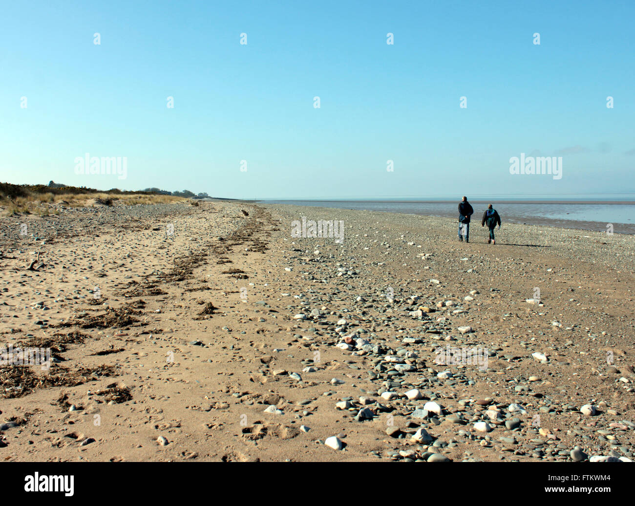 Two people walking along the wide open shore line under a cloudless ...