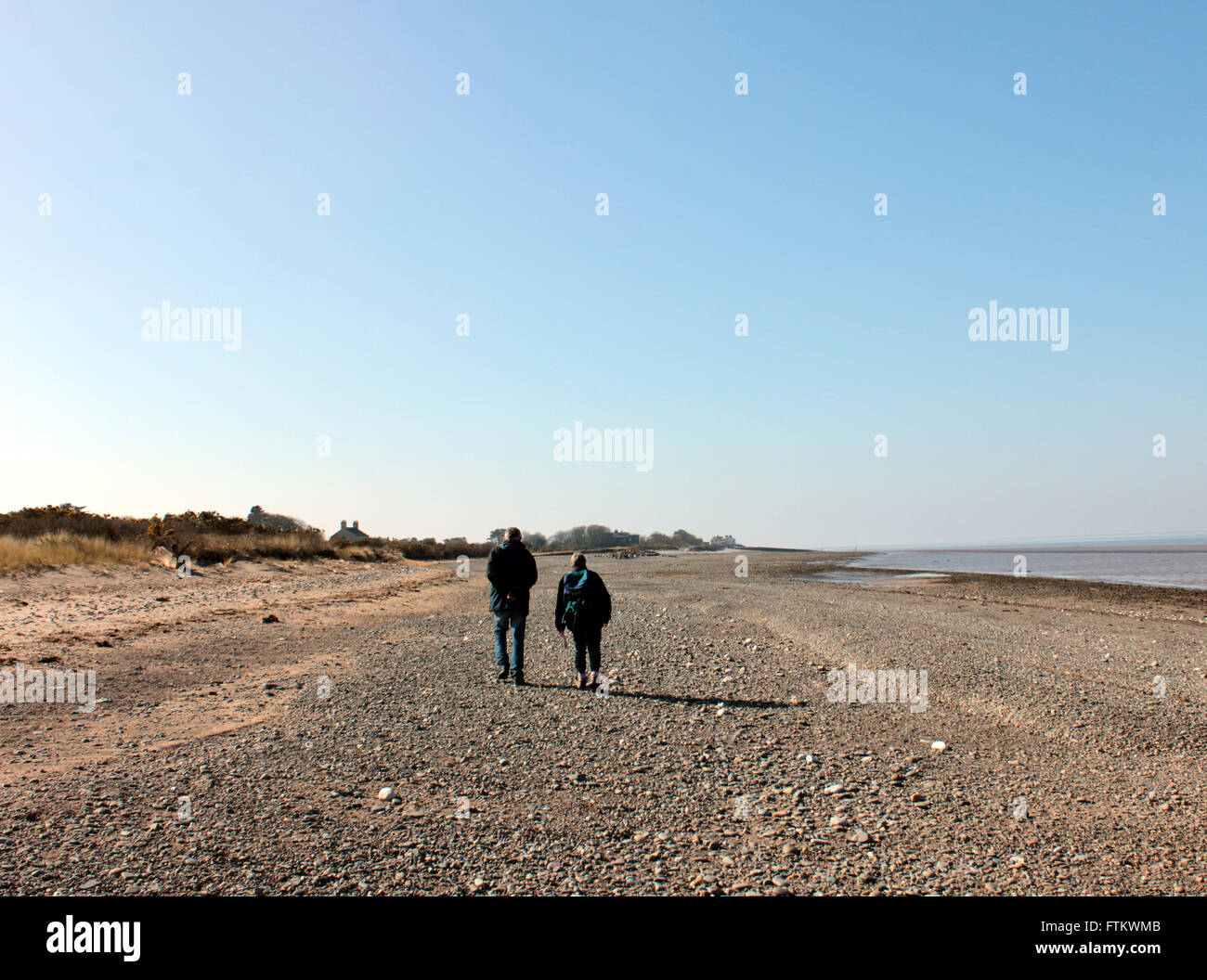 Two people walking along the wide open shore line under a cloudless ...