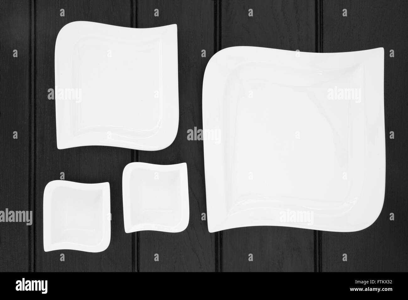 Square shaped modern plates of varying sizes over dark wood background ...