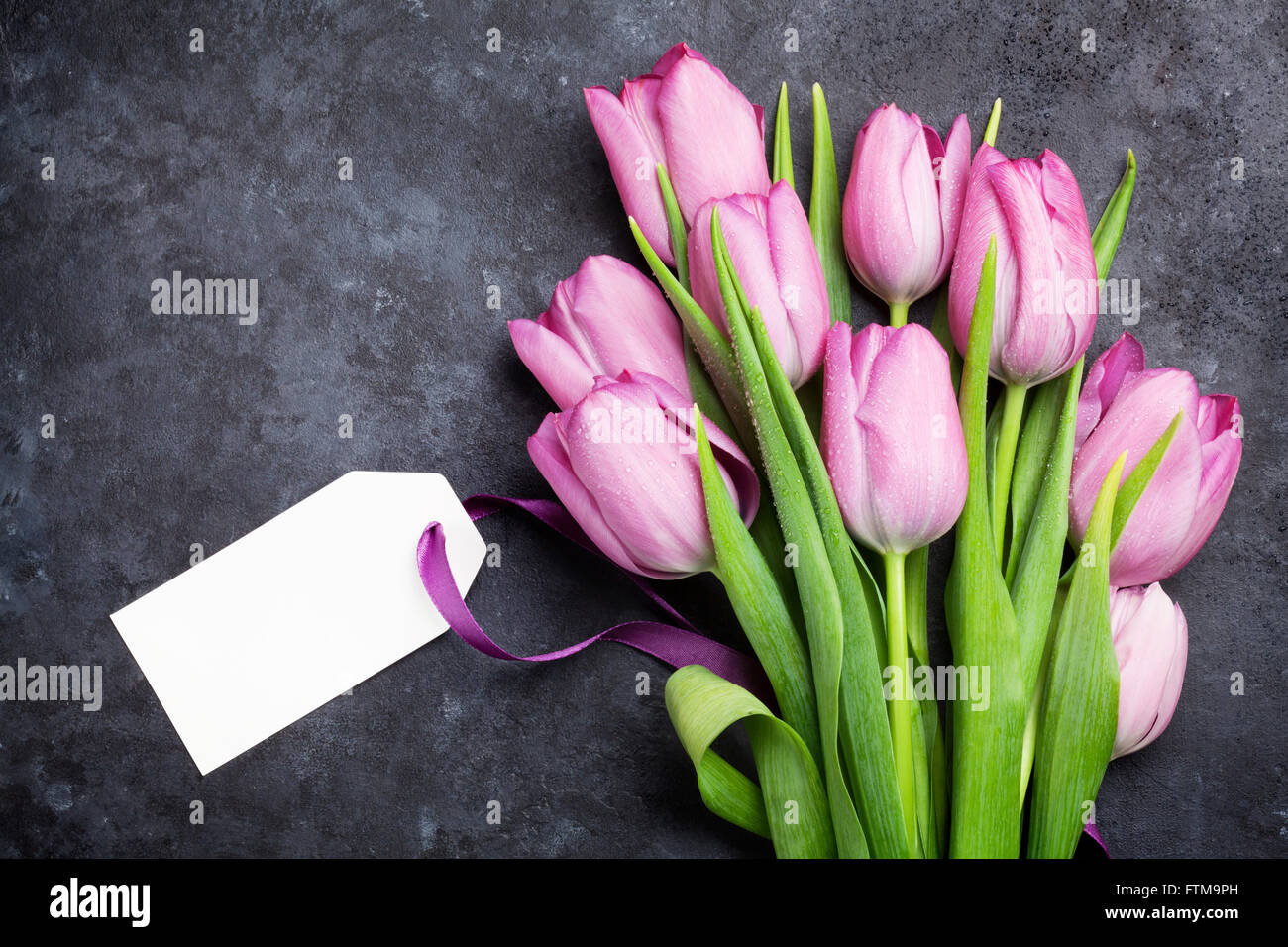 Fresh purple tulip flowers with tag label on dark stone table. Top view ...