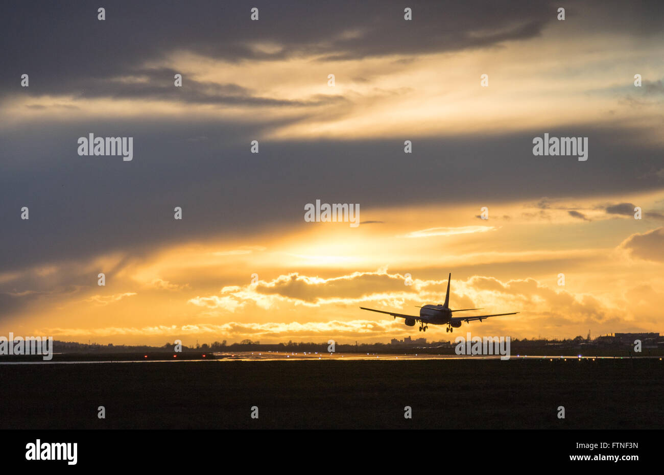 A Boeing 737 is silhouetted against clouds illuminated by the setting ...