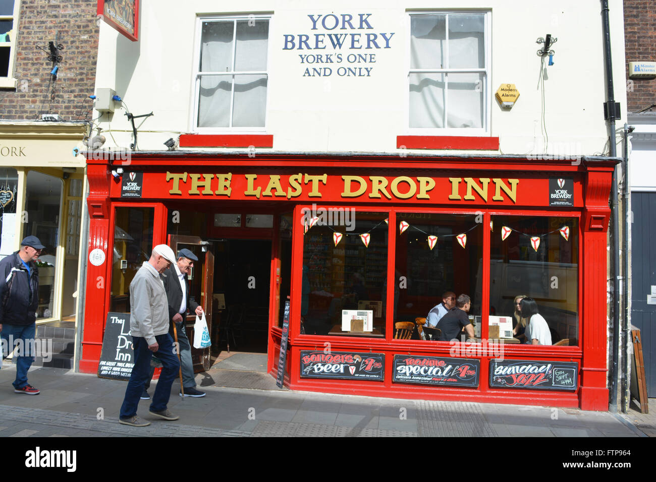 Men walking past The Last Drop Inn, with group of people sitting inside ...