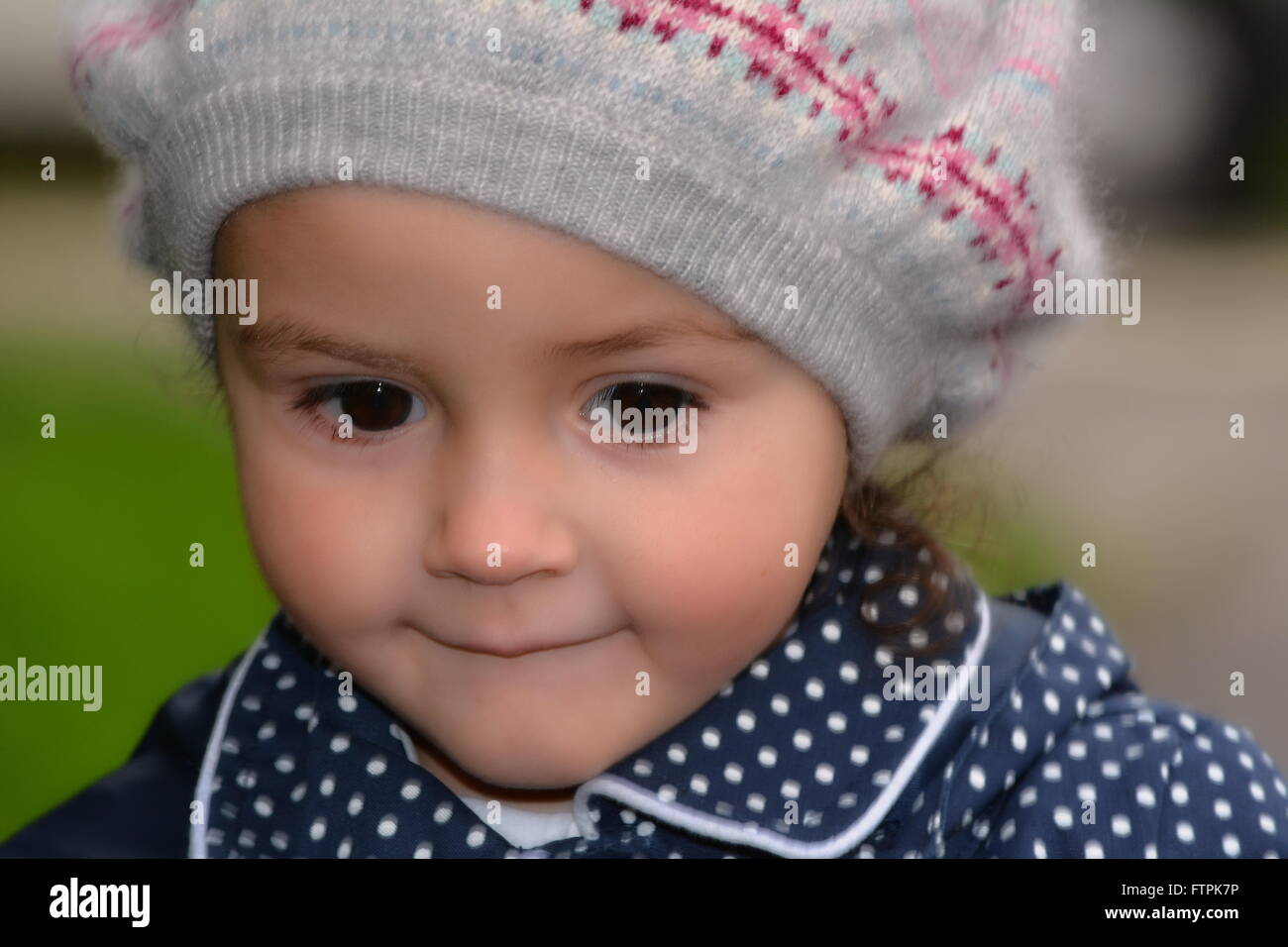 Young girl wearing warm wool hat with cheeky smile. A small child looks ...