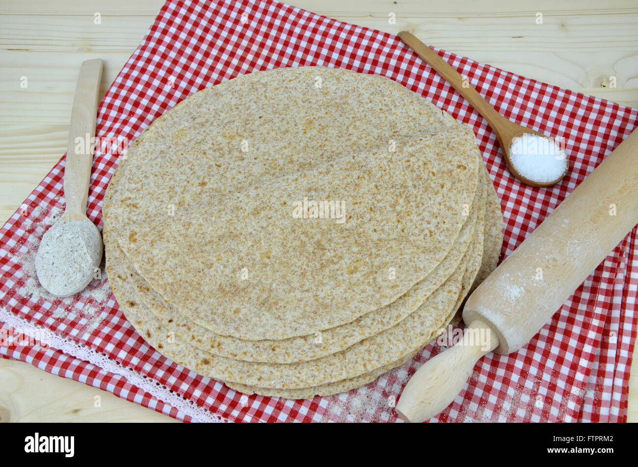 Tortillas set on red-white tablecloth with wooden rolling pin and ...