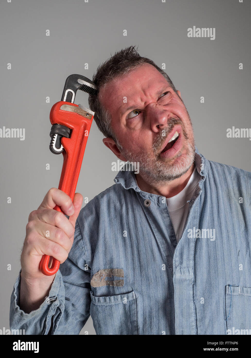 Photograph of a repairman in blue coveralls looking confused and ...