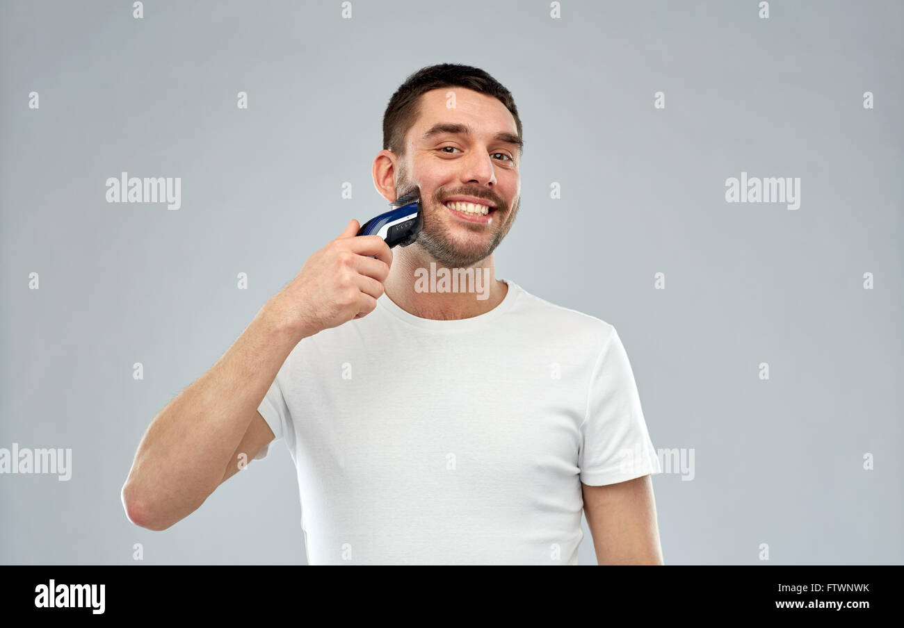 smiling man shaving beard with trimmer over gray Stock Photo - Alamy