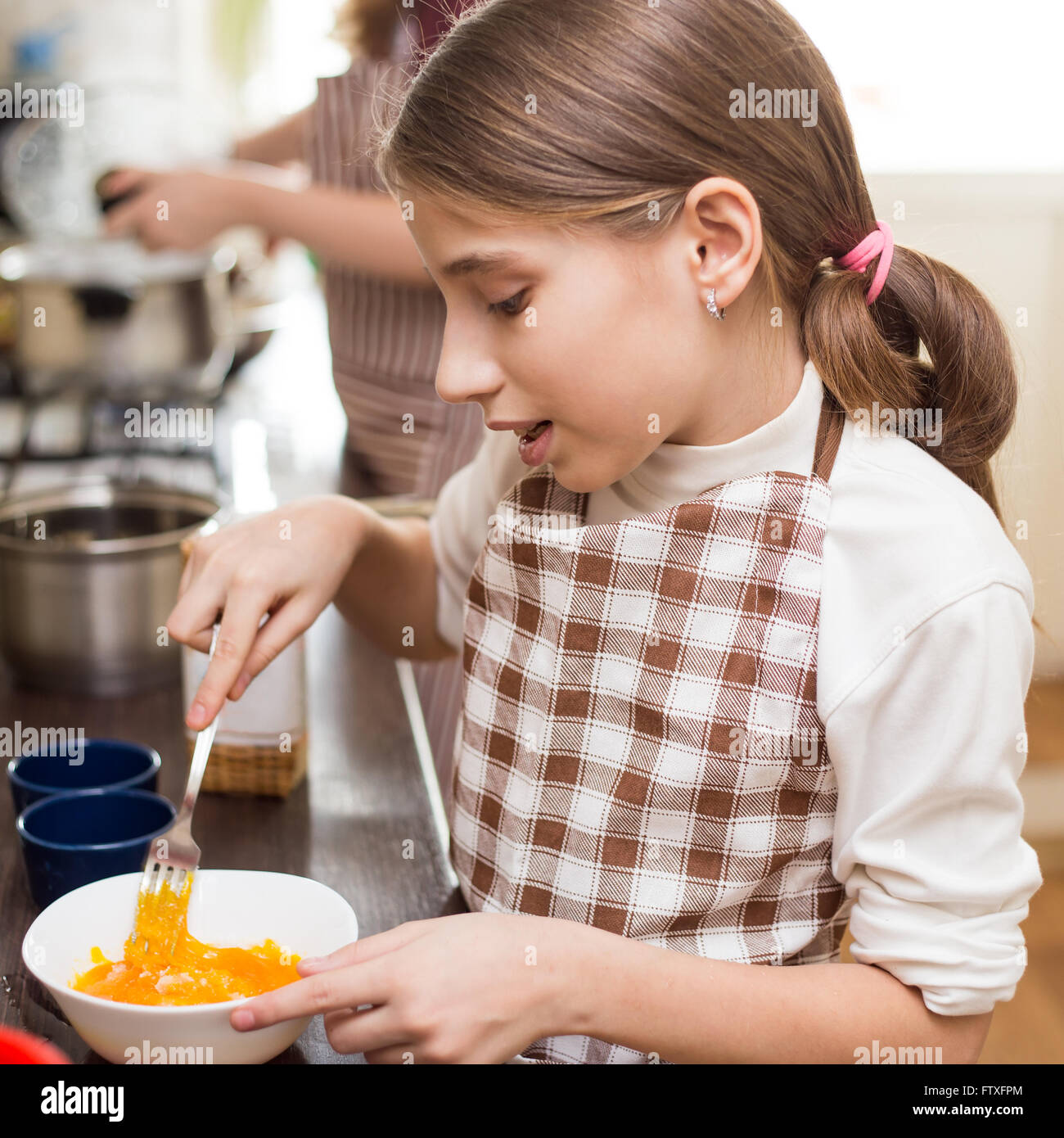 Small teenage girl in apron whisking eggs in white bowl in the kitchen ...
