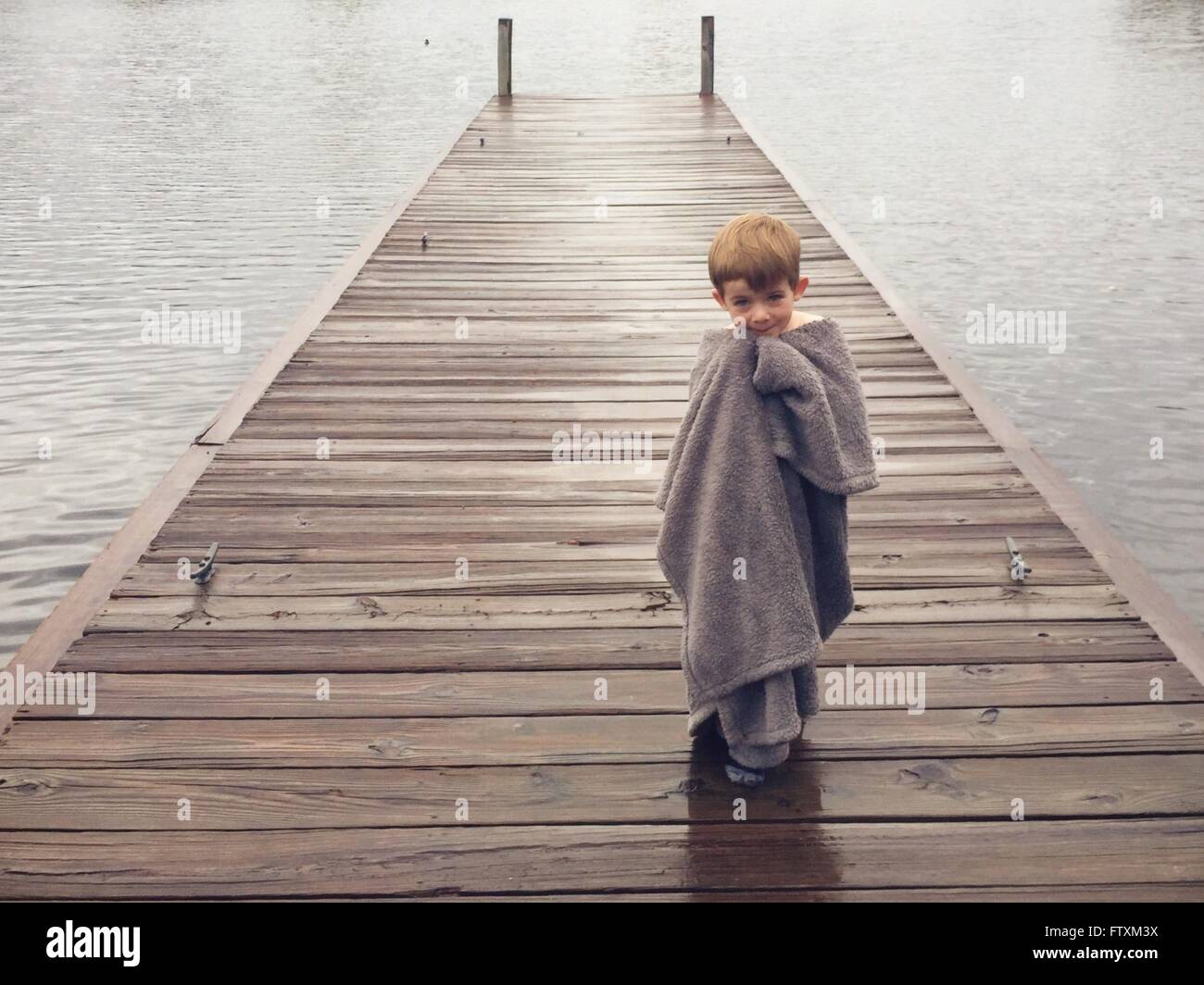 Boy wrapped in blanket, standing on pier Stock Photo - Alamy