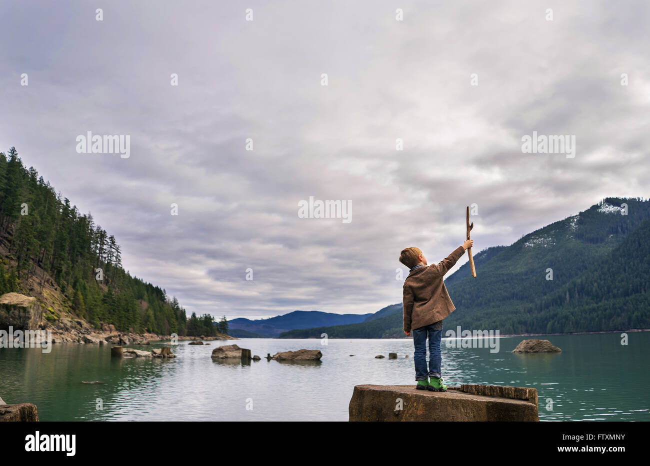 Boy standing on rocks by river holding stick Stock Photo - Alamy