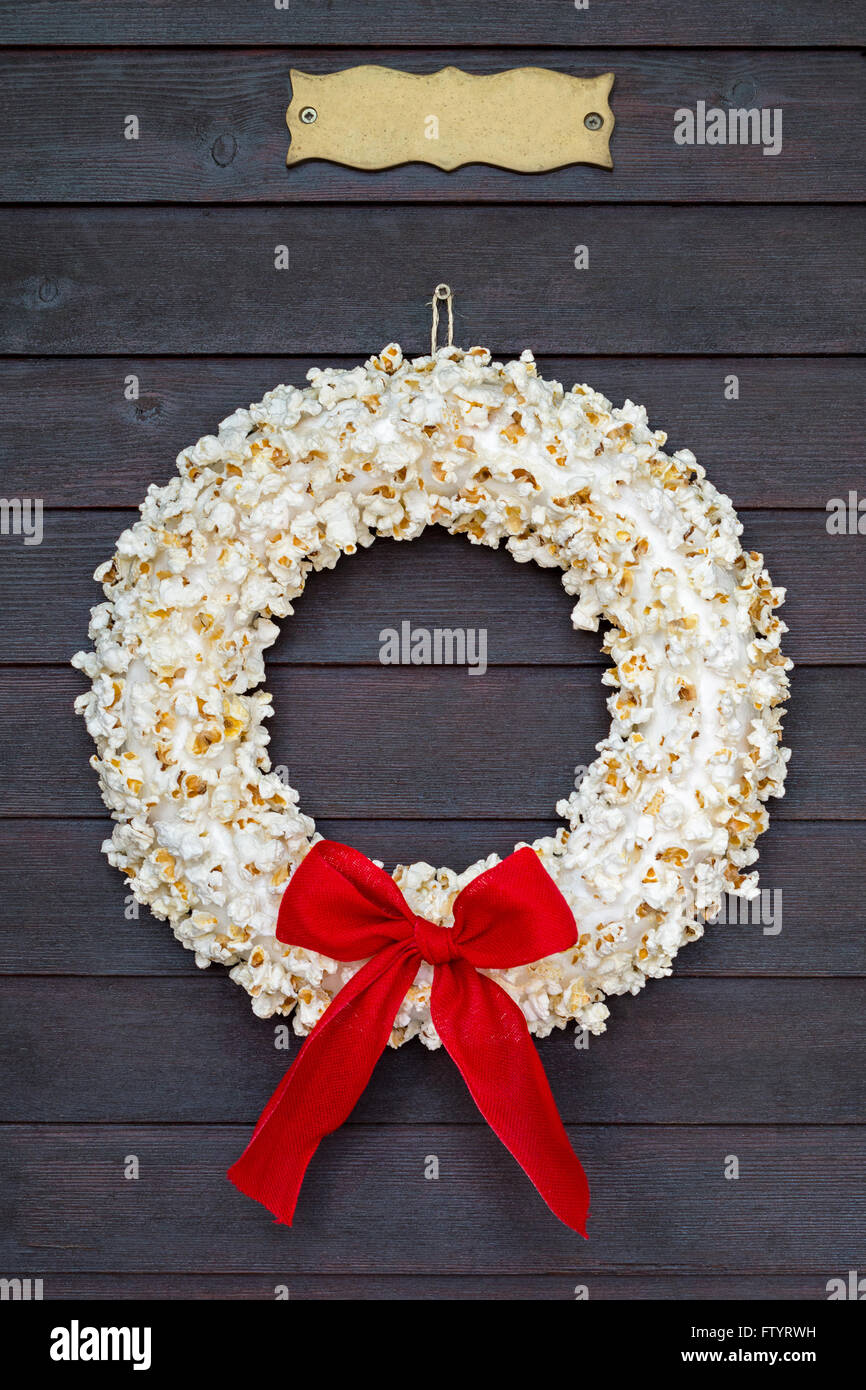 Popcorn wreath with red bow hanging on dark wooden door with name plate ...