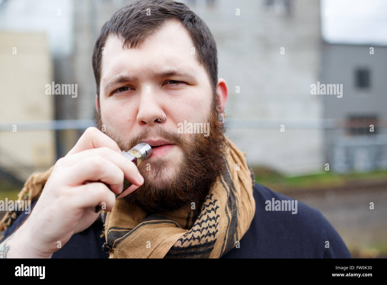 Urban lifestyle portrait of a man vaping in an urban environment with a ...