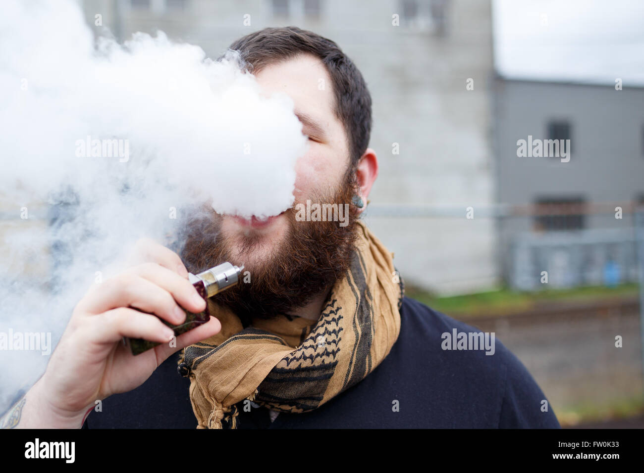 Urban lifestyle portrait of a man vaping in an urban environment with a ...