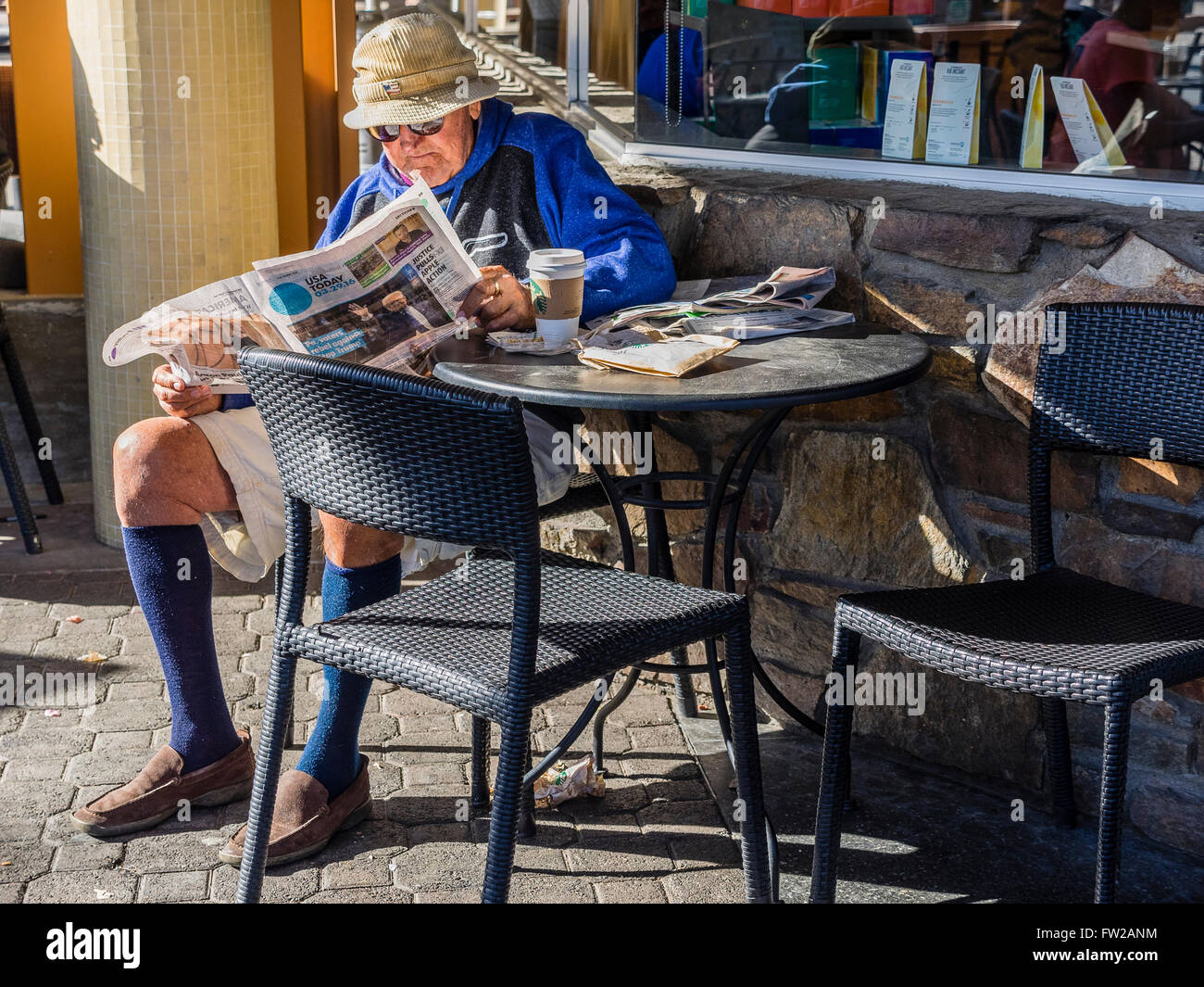 Male senior citizen reading a newspaper at a coffee shop in early ...