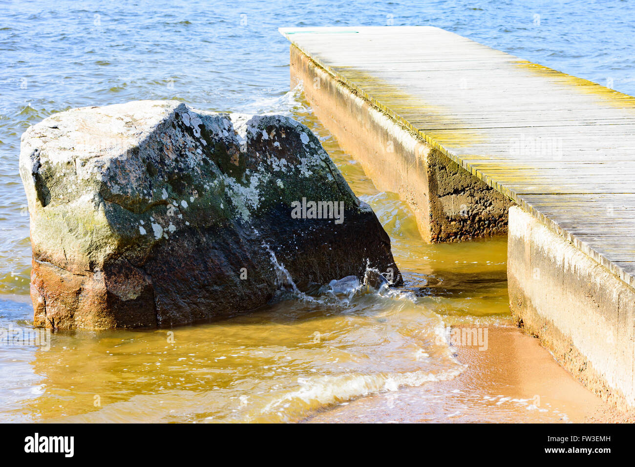 A big granite rock beside a wooden and concrete pier. The pier has a ...