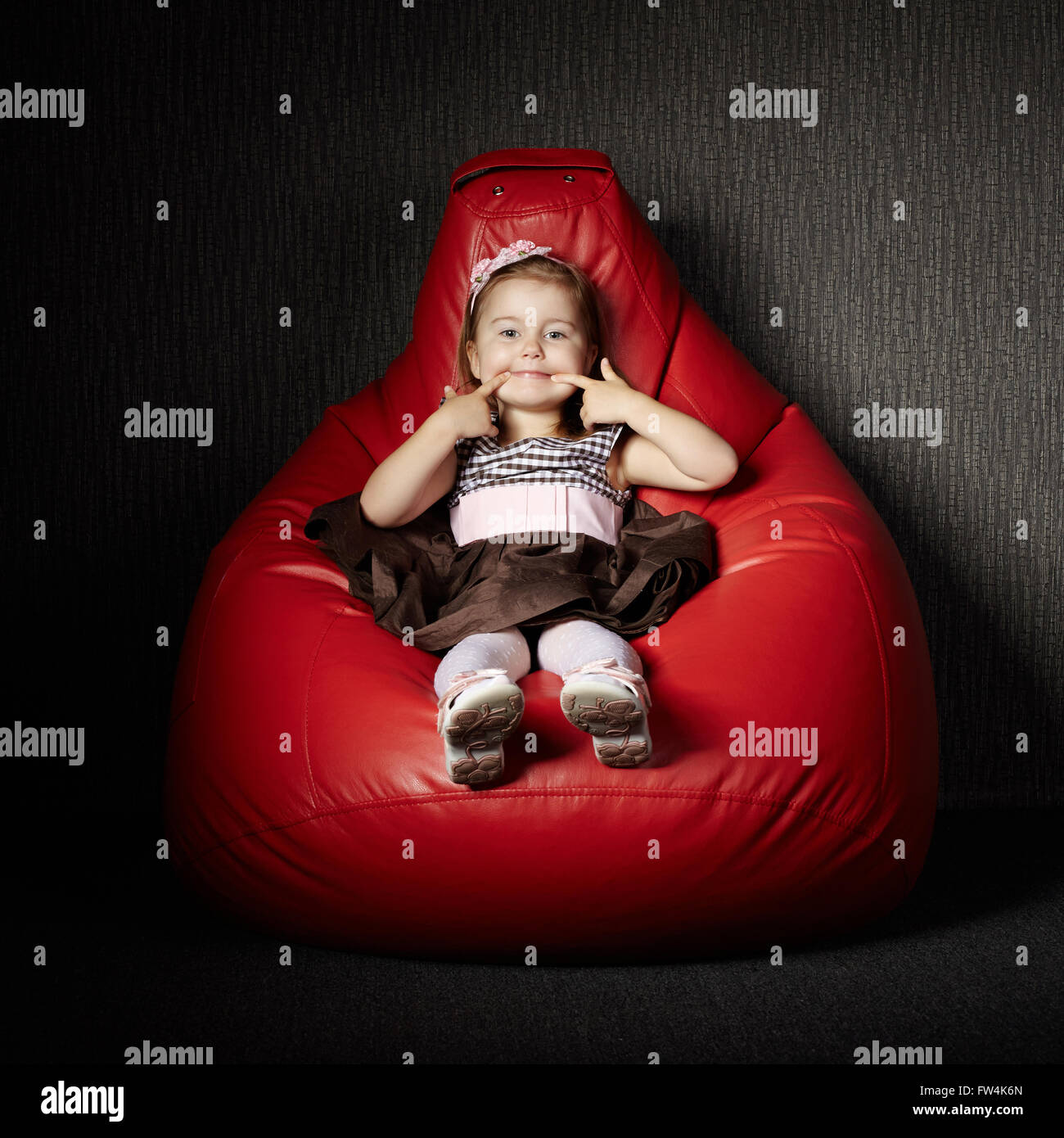 Little girl sitting on red beanbag Stock Photo - Alamy
