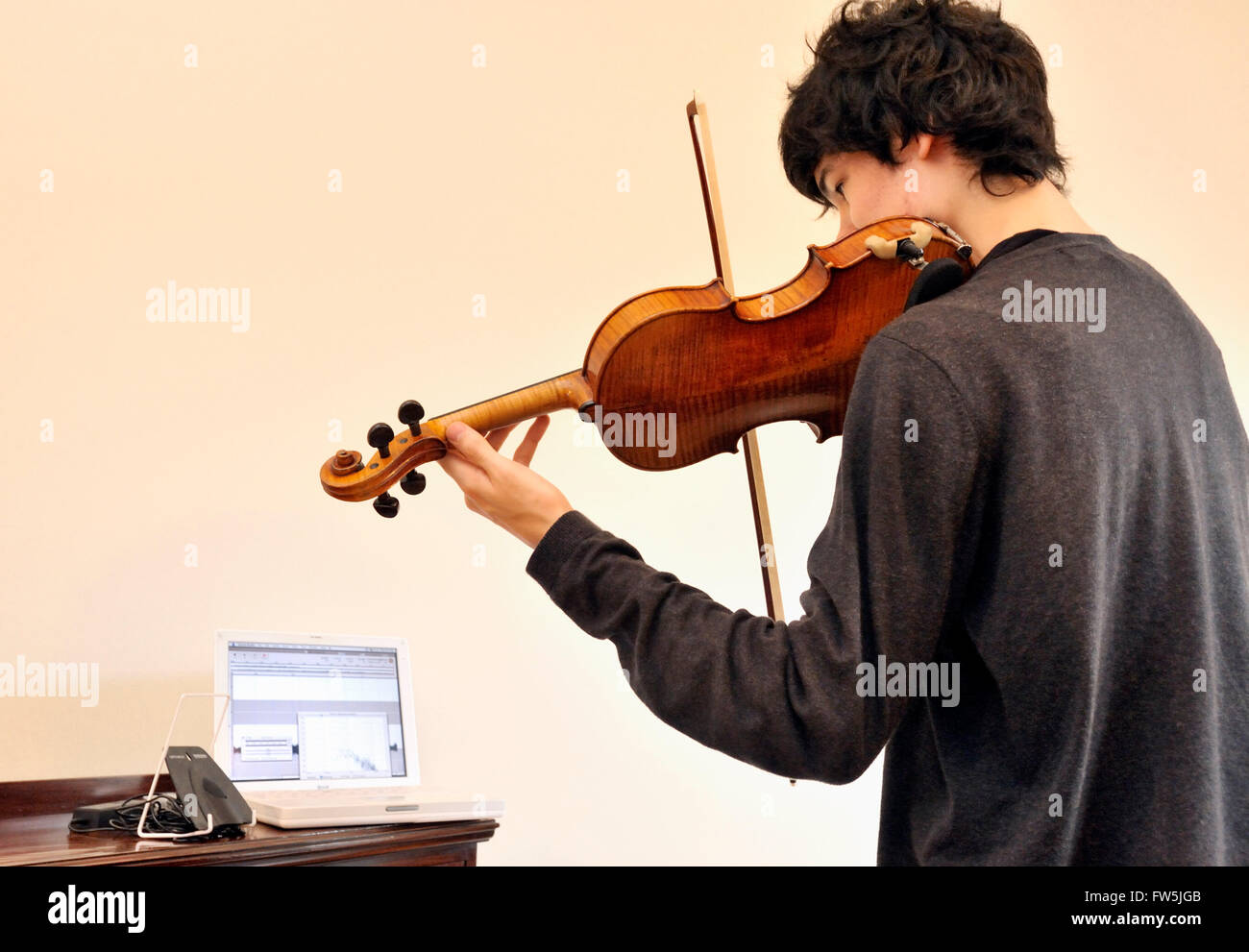 Teenage boy making a recording, playing the violin, with computer ...