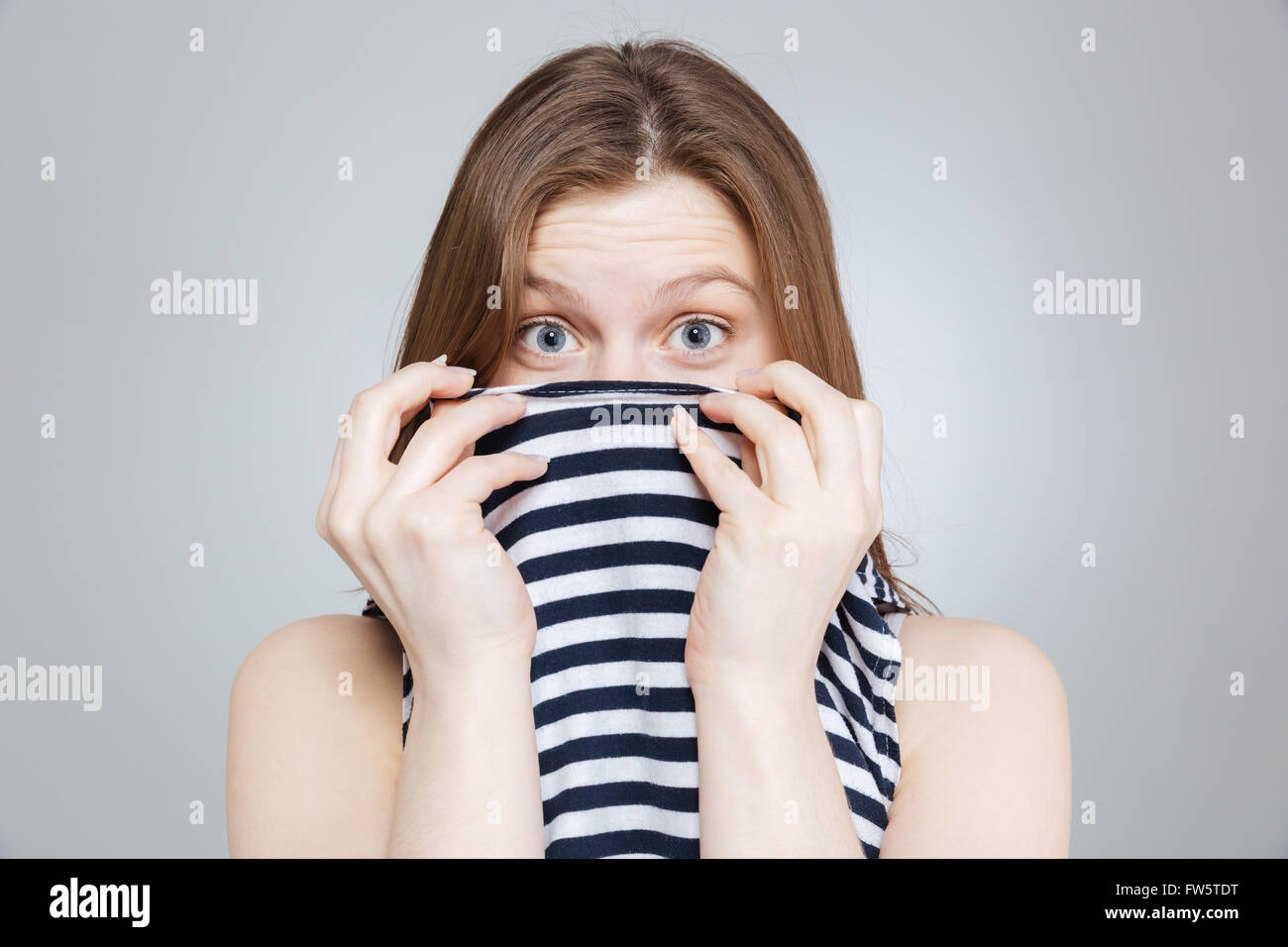 Scared shocked teenage girl covered her face with striped top over gray ...