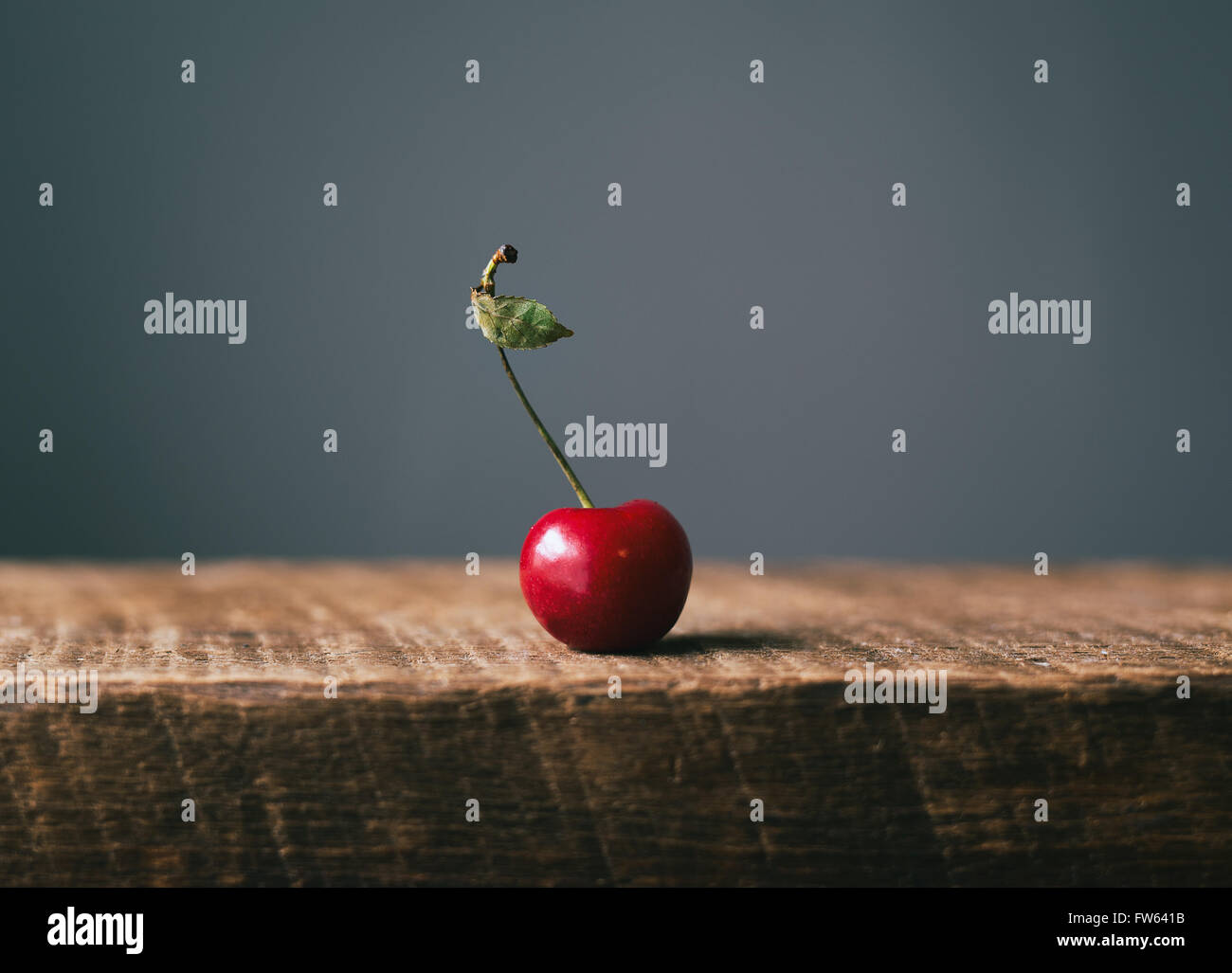 Single cherry on rustic wooden table Stock Photo - Alamy