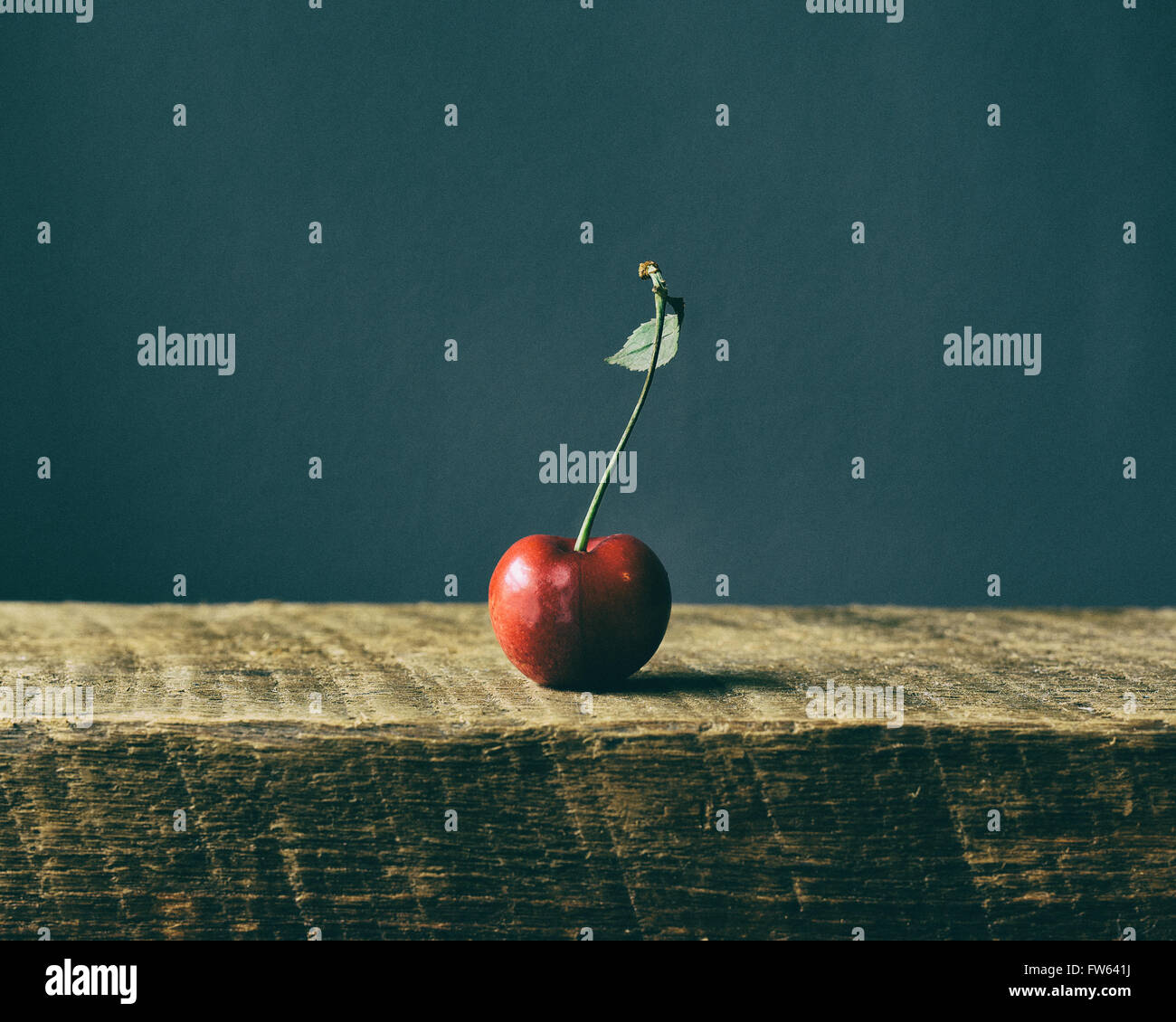 Single cherry on rustic wooden table Stock Photo - Alamy