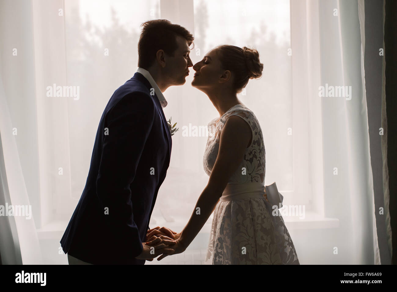 Happy newlyweds kissing indoor. Brunette bride and groom stand near ...