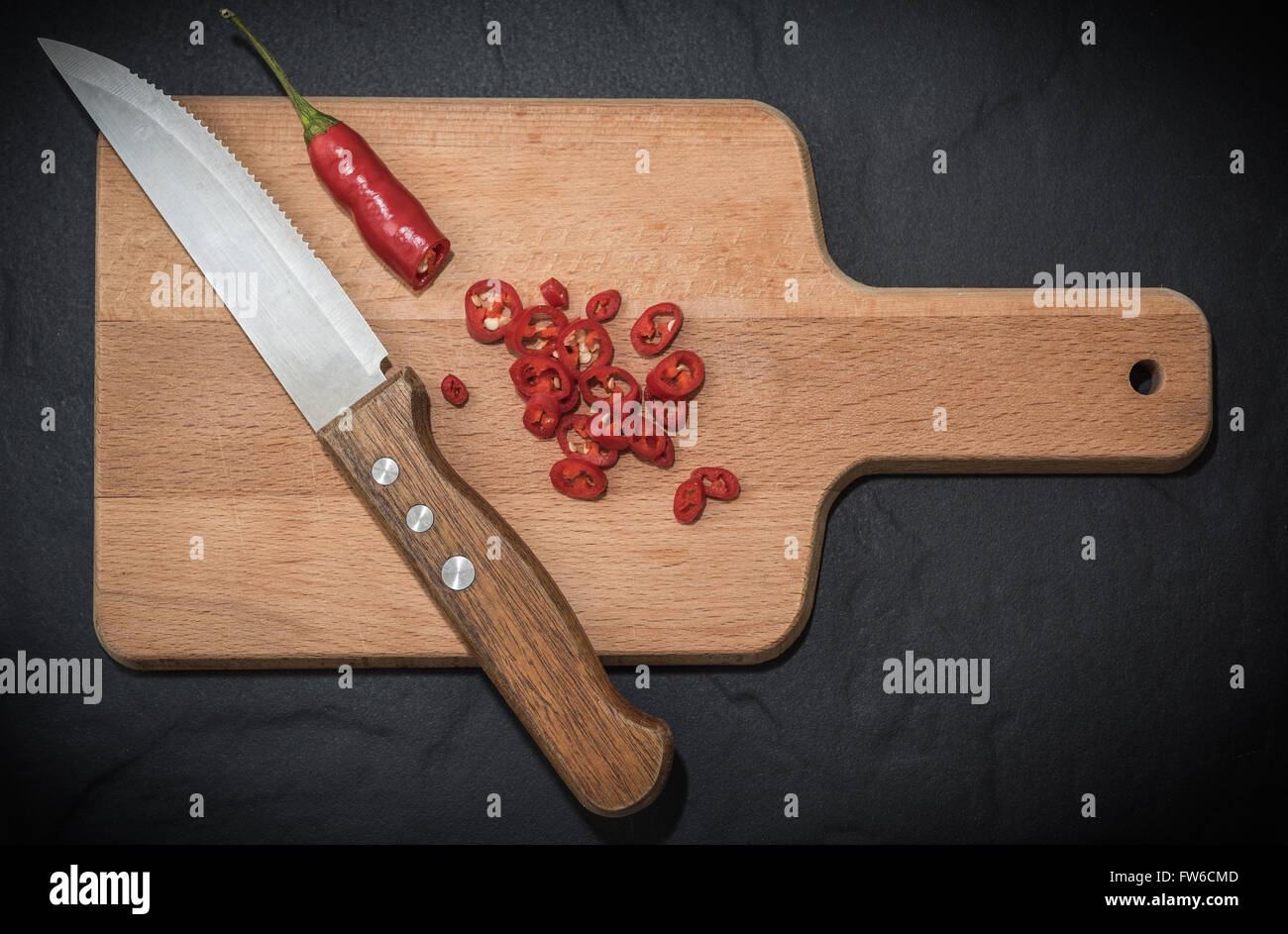 Rustic wooden chopping board on a Black slate background red chili ...