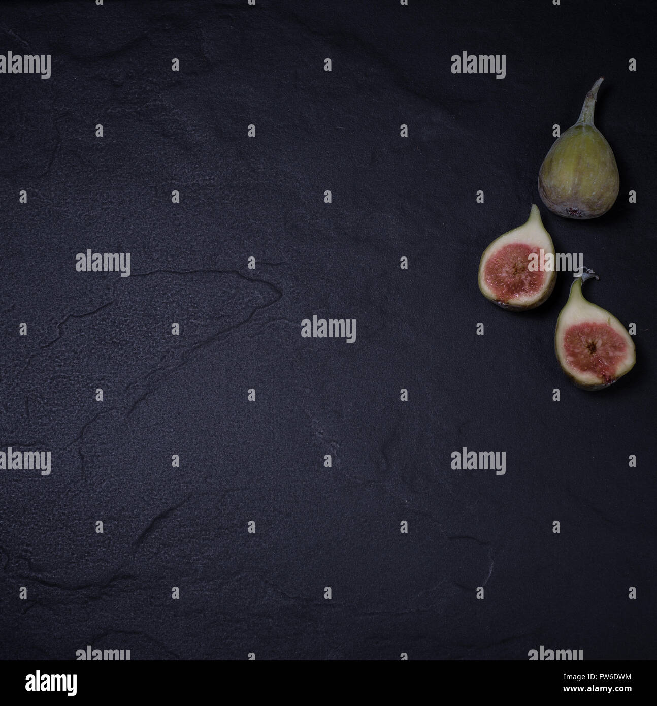 Top down shot of fresh figs with green tops on a black slate background ...